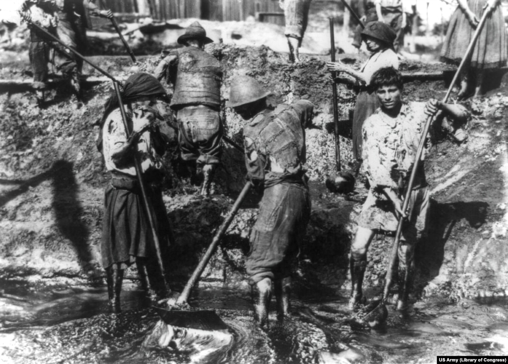 Workers scoop out gloppy ladles of oil from a storage pool at an ...